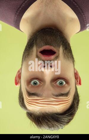 Astonished, shocked. Inverted portrait of caucasian young man on yellow ...