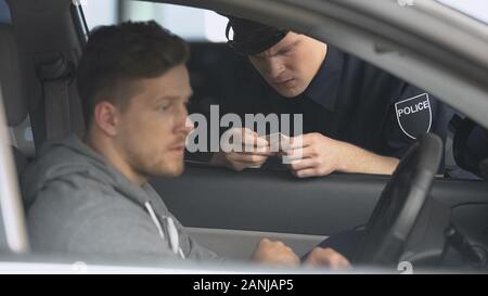 Serious policeman checking male drivers license after exceeding speed ...