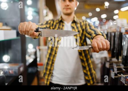 Young man holds kitchen knives in houseware store. Male person buying ...