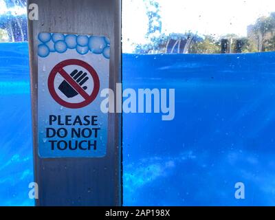 A warning sticker on a post that says Please Do Not Touch on a aquarium ...