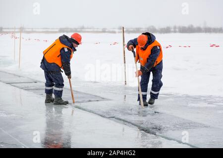 Workers rafting ice blocks along a channel cut out by a frozen lake ...