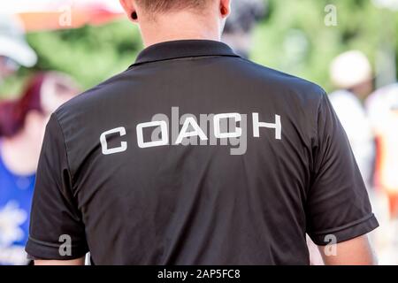 Back view of a male coach wearing black coach shirt with the white word ...