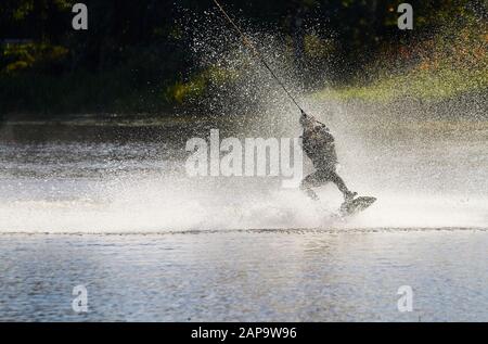 Wakeboarder surfing across a lake with water splashing. This is an ...