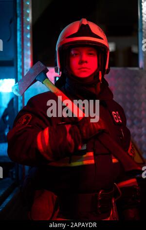 Firefighter male with hammer on his shoulder standing near fire engine ...