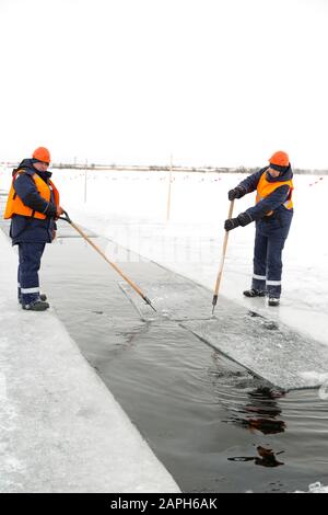 Workers rafting ice blocks along a channel cut out by a frozen lake ...