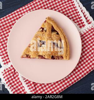 triangular slice of baked cherry pie on brown paper, top view, blue ...