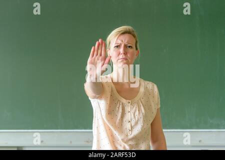 Angry and upset female teacher standing in class against clean green ...