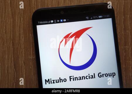 Smartphone with Mizuho Financial Group logo on screen in clenched hand ...