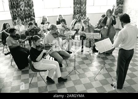 Secondary School 1990s UK. Teacher sitting on desk, one asian student ...