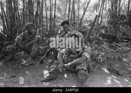 Three KNIL soldiers in camouflage uniform stand by a lying tree trunk ...