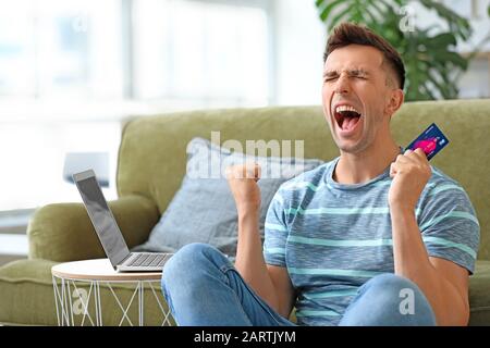 Happy young man with credit card in hand shopping online on laptop ...