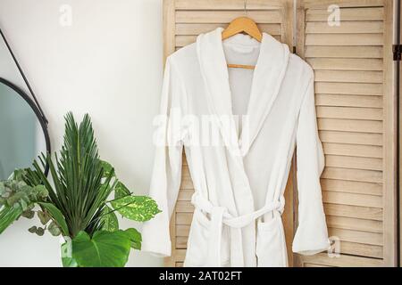 White bathrobe hanging on folding screen against yellow background ...