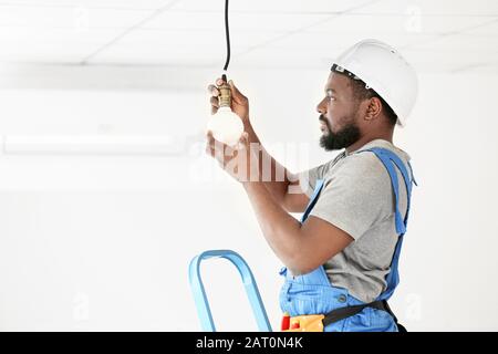African-American electrician performing wiring in distribution board ...