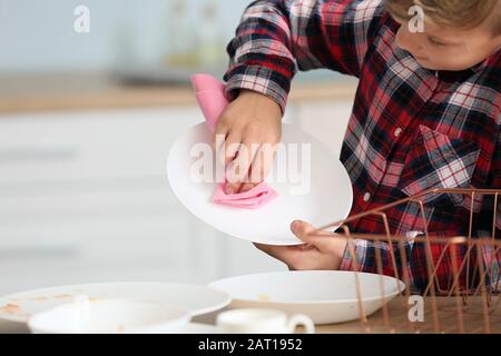 Child doing and wiping dishes in kitchen. Little kid cleaning at home ...