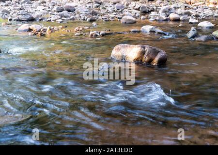 beautiful ripples on river flow over colorful stones in summer sunshine ...