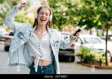 Excited girl listen music in headphones and looking at smartphone ...