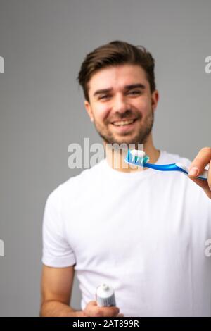 Young man showing toothbrush with toothpaste isolated, guy holding ...