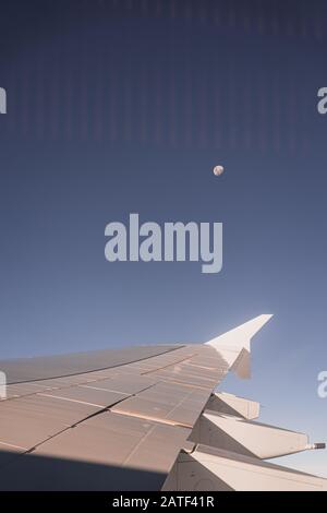 airplane wing through the airplane window with the moon in the ...