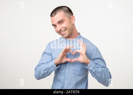 Hopeful man in love showing red heart sign, smiling at camera, waiting ...