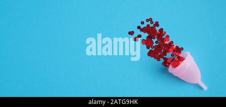 Reusable menstrual cup filled with red confetti on pink background ...