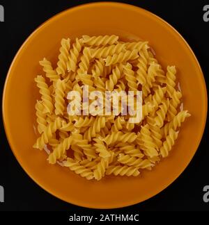 Uncooked Fusilli Pasta Lying on White Plate on Black Background. Raw ...