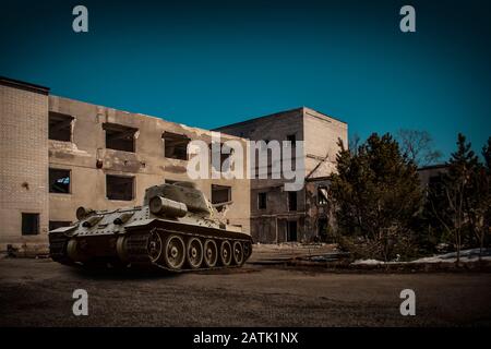 A war scene of a single tank cruising in the city by a big demolished ...