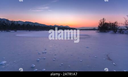 A landscape of a frozen pond surrounded by trees covered in the snow in ...