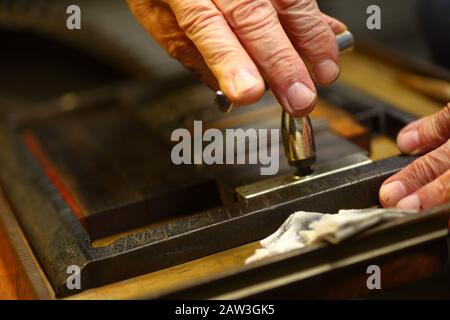 Closeup of ink-stained fingers of man using a quoin key to prepare type ...