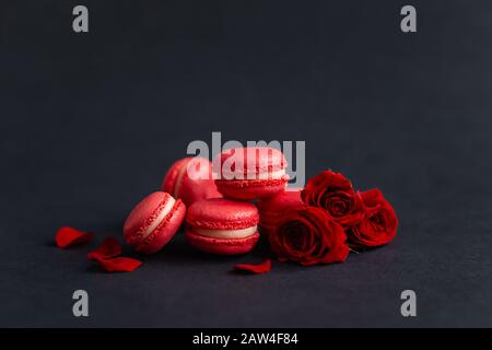 Tasty french macarons with red roses on a black background. Concept for ...