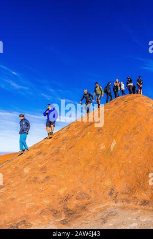 Tourists climb over the steep undulating terrain on top of Uluru ...