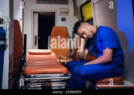 Tired corpsman in medical uniform sits inside the ambulance car at ...