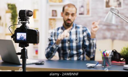 Vlogger sitting at desk in living room talking and looking at the ...