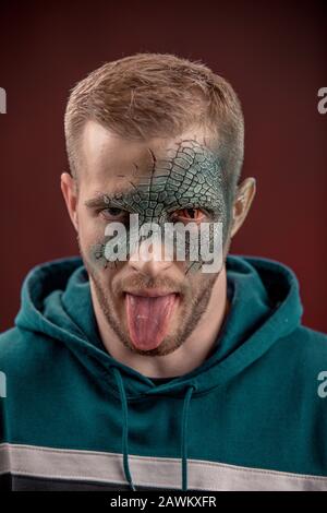 man with professional horror movie make-up green lizard on dark red ...