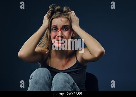 Scared blonde girl, bleeding face covered with bruises, in black ...