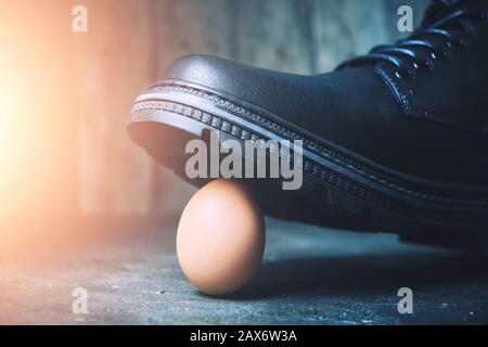 Black boot steps on a fragile chicken egg. The concept, the weak ...