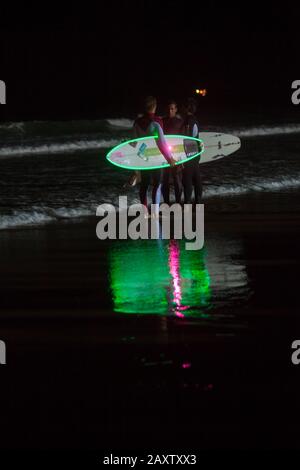 Surfers going surfing with neon surfboards at night Stock Photo - Alamy
