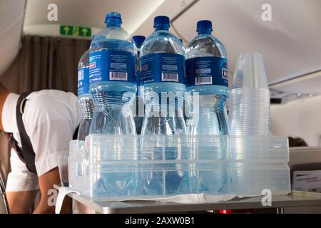 Member of cabin crew with water drinks trolley looks through curtains ...