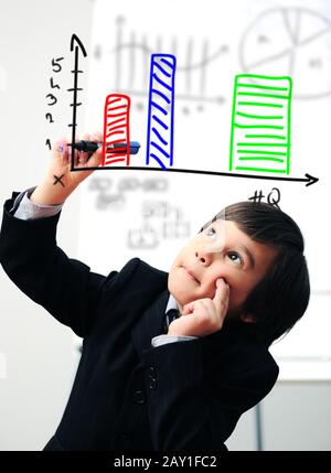 Portrait of cute boy with sketch pen and paper at desk in classroom ...