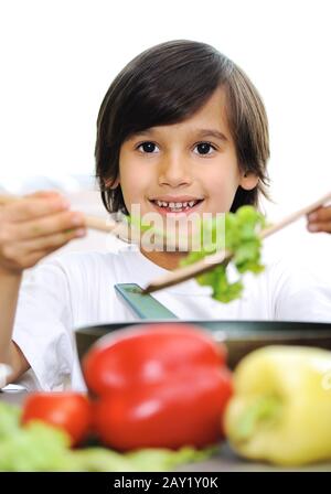 Young boy standing and cooking vegetables at table with adorable white ...
