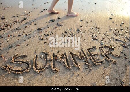 The word "summer" written on the sand by the sea at sunset while a wave ...