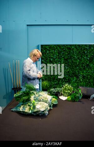 A mature blonde woman arranging plants in an indoor flower shop setting ...