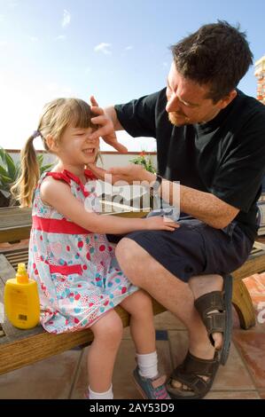 Parent caring for child applying sun protection cream on face outdoors ...