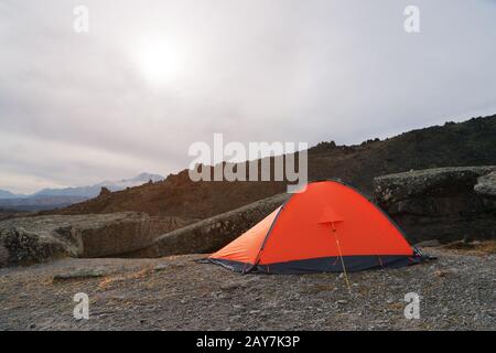 An orange high-altitude tent is set between stones high in the ...