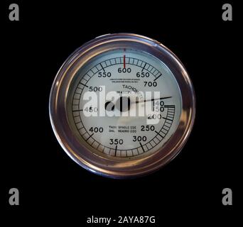 An old round metal industrial tachometer on a black background with ...