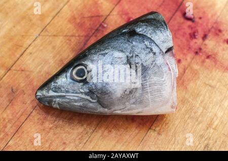 Cut head of raw mackerel fish with blood on wooden board surface ...
