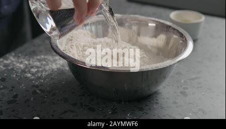 man adds wet ingredients into flour in steel bowl on concrete ...