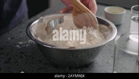 man mixing dry ingredients with flour in steel bowl on concrete ...