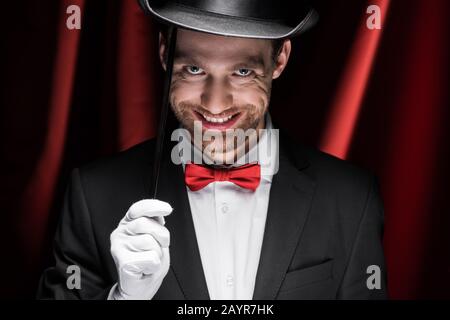 handsome scary magician in suit and hat holding wand in teeth in circus ...