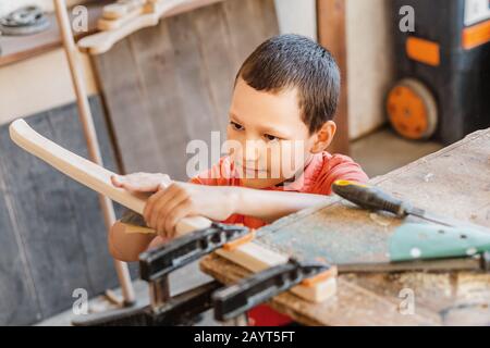 Little talented genius boy works with wood in a carpentry workshop. The ...