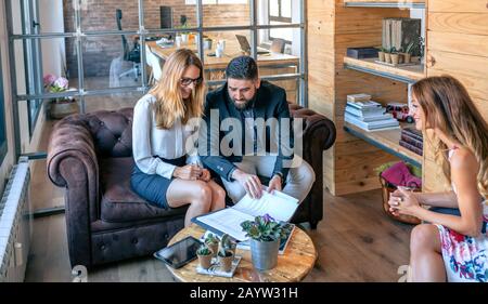 Three young happy businesspeople having a meeting while sitting at a ...